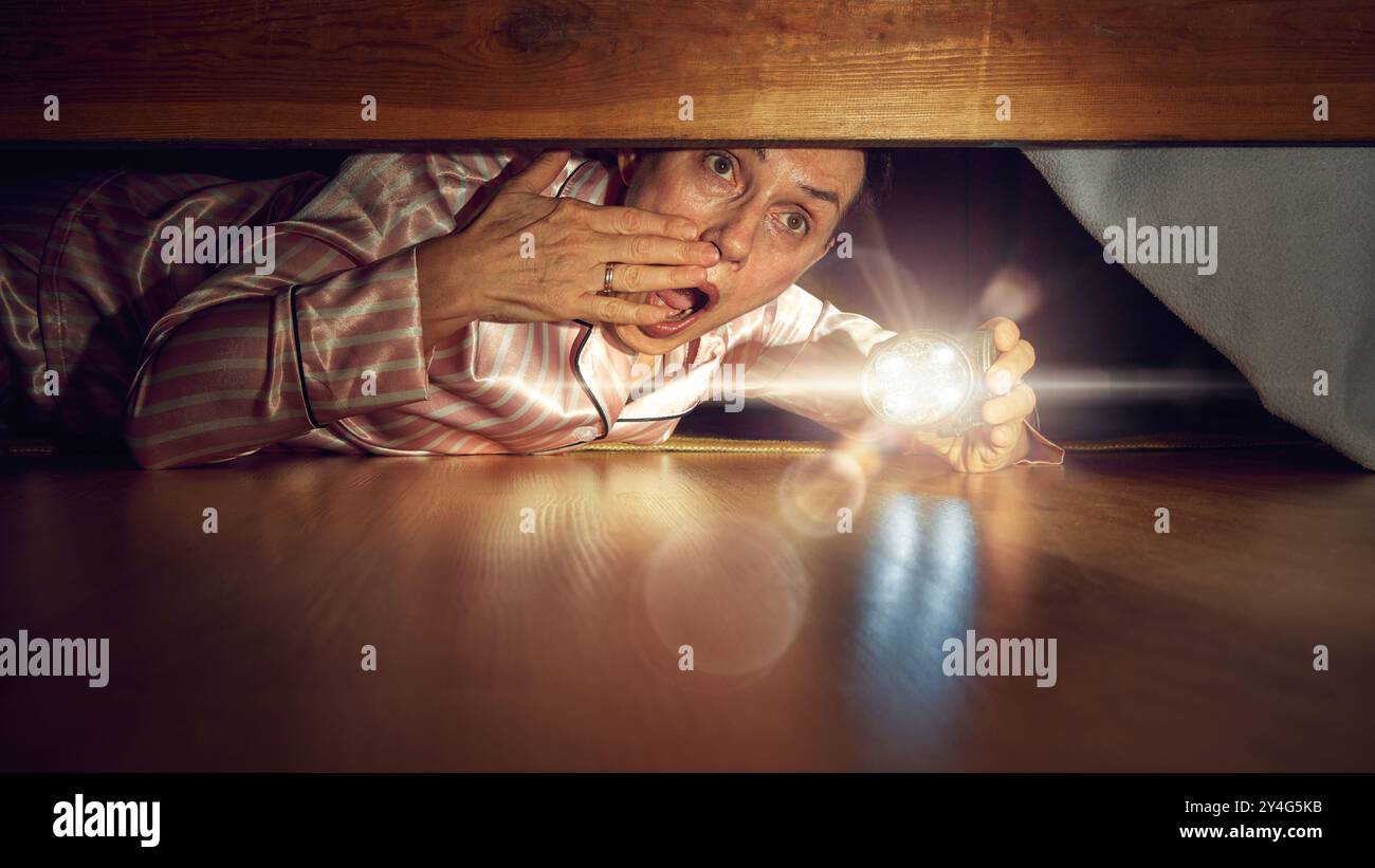 Senior woman with emotional face, lying on floor and looking under bed ...