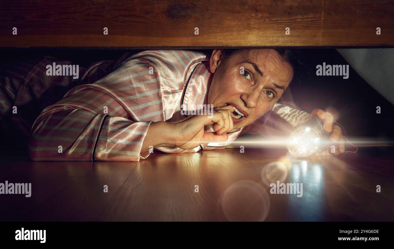 Senior woman with emotional face, lying on floor and looking under bed ...