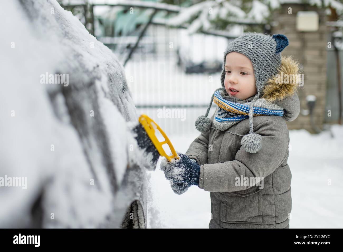 Adorable little boy helping to brush a snow from a car. Mommy's little ...