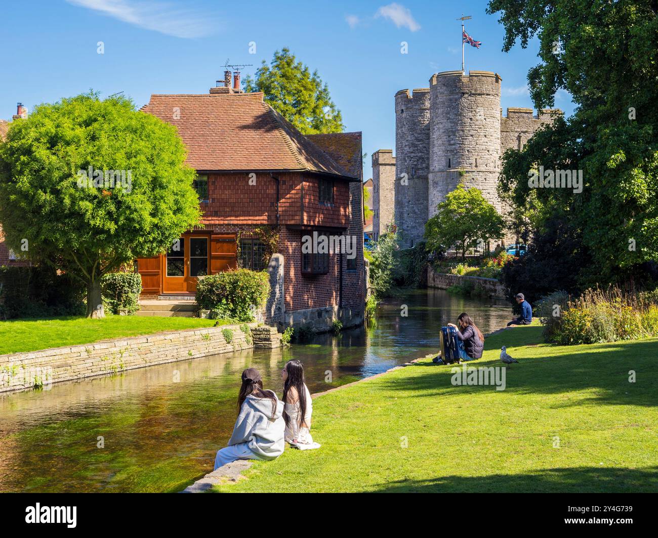 People sitting next to Great Stour, Westgate Gardens, with Westgate ...