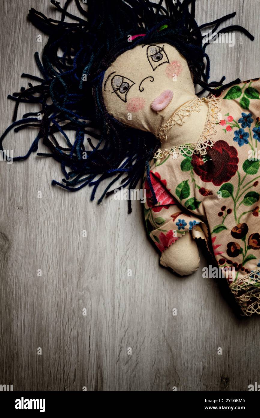 Old rag doll with blue yarn hair lies peacefully on a rustic wooden ...