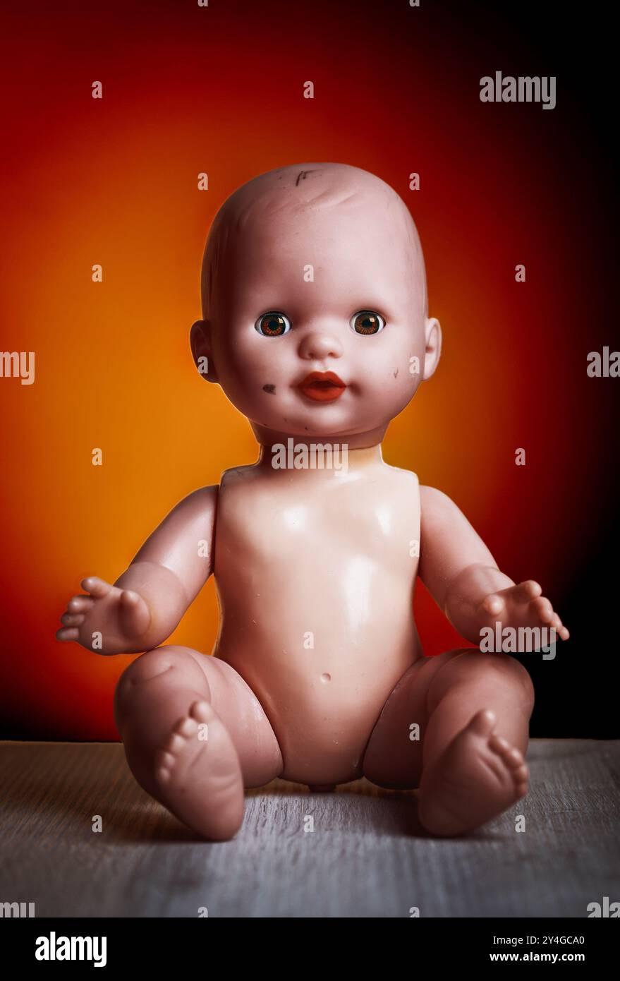 Creepy baby doll sits alone on a table, casting eerie shadows against a ...