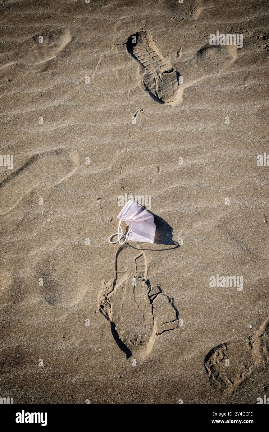 Surgical mask is laying on the sand with footprints surrounding it ...