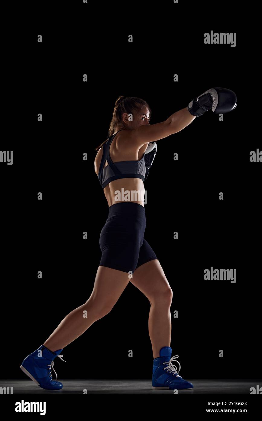 Focused young woman with fit body, boxing athlete in motion in gloves ...