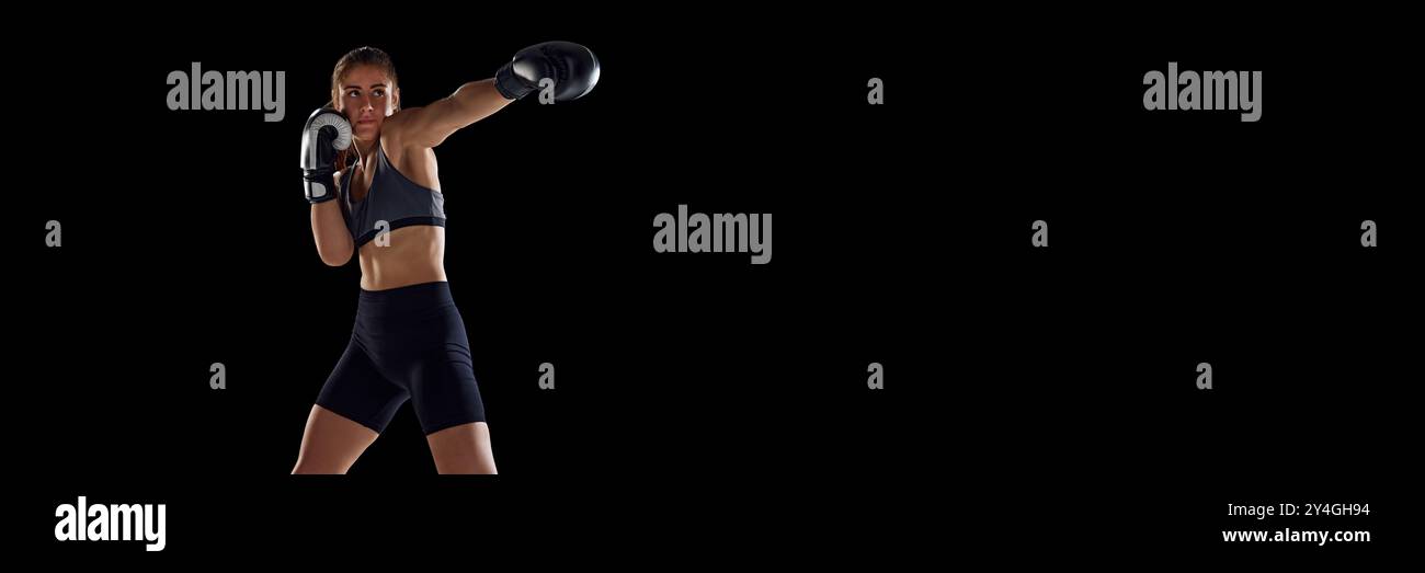 Focused young woman with fit body, boxing athlete in motion in gloves ...