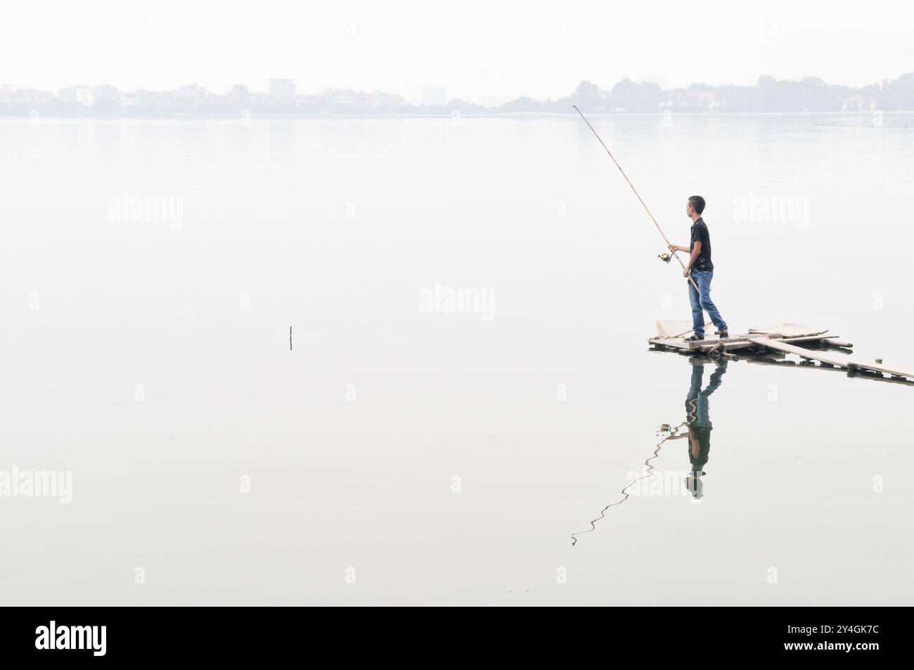 A fisherman stands on a narrow wooden jetty to cast his line from a ...