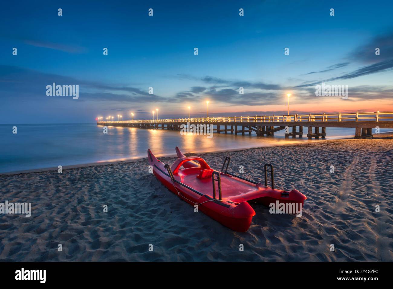 The pier of Forte dei Marmi and a lifeguard rowing catamaran at sunset ...