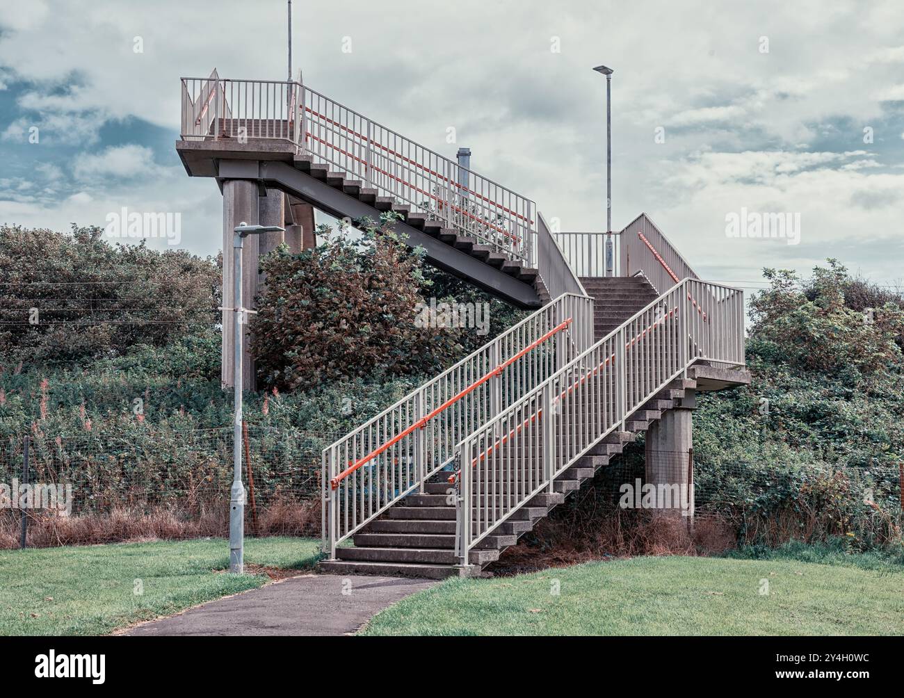 A brutalist stepped pedestrian walk way bridge is built over a railway ...