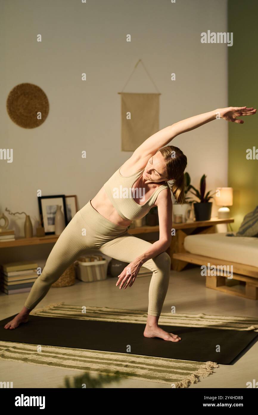 Young fit woman in beige activewear standing on mat at home and doing ...