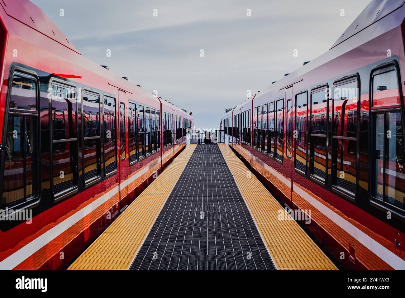 Two red trains on a station platform with yellow safety lines and a ...