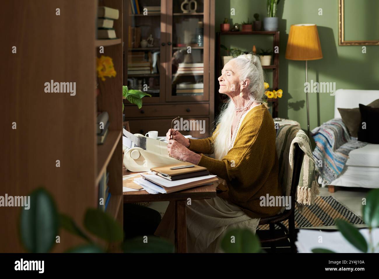 Elderly woman writing at wooden desk surrounded by bookshelves and ...