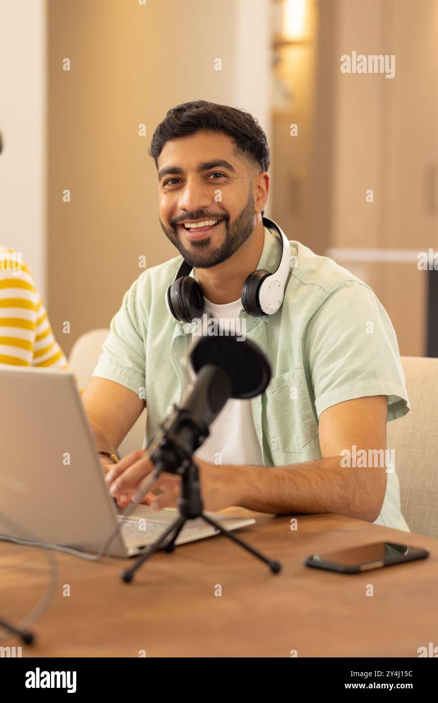 Using laptop and microphone, man smiling while working from home office ...