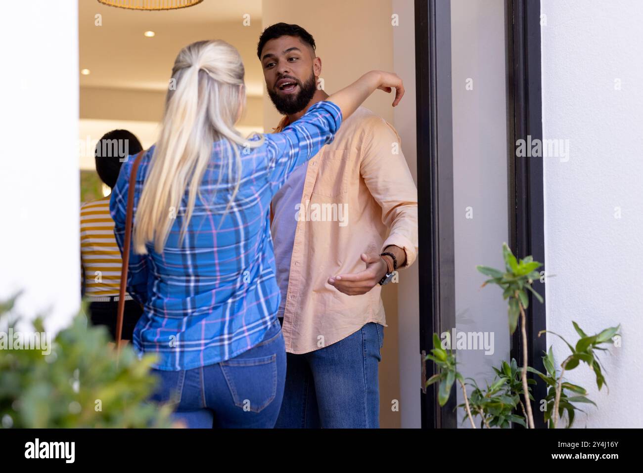 Friends greeting each other with hug at home entrance, smiling warmly ...