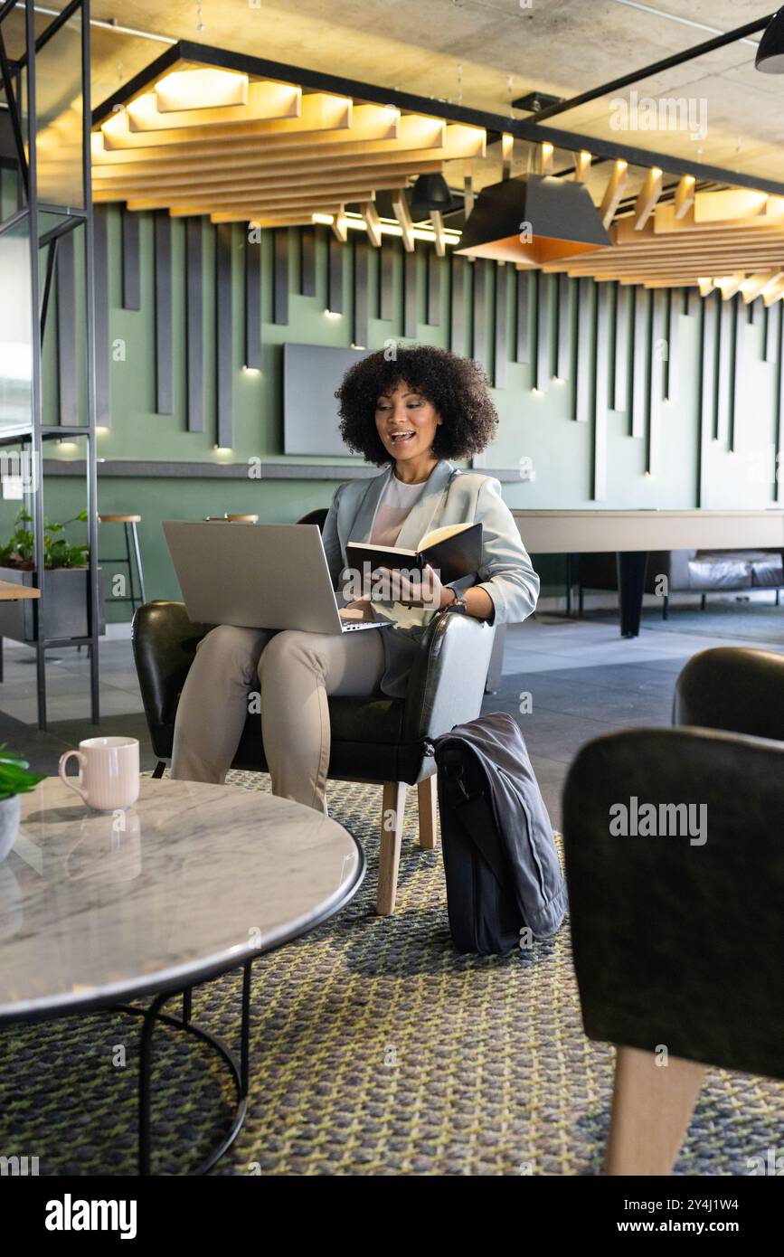Holding laptop and notebook, woman working in modern office lounge area ...