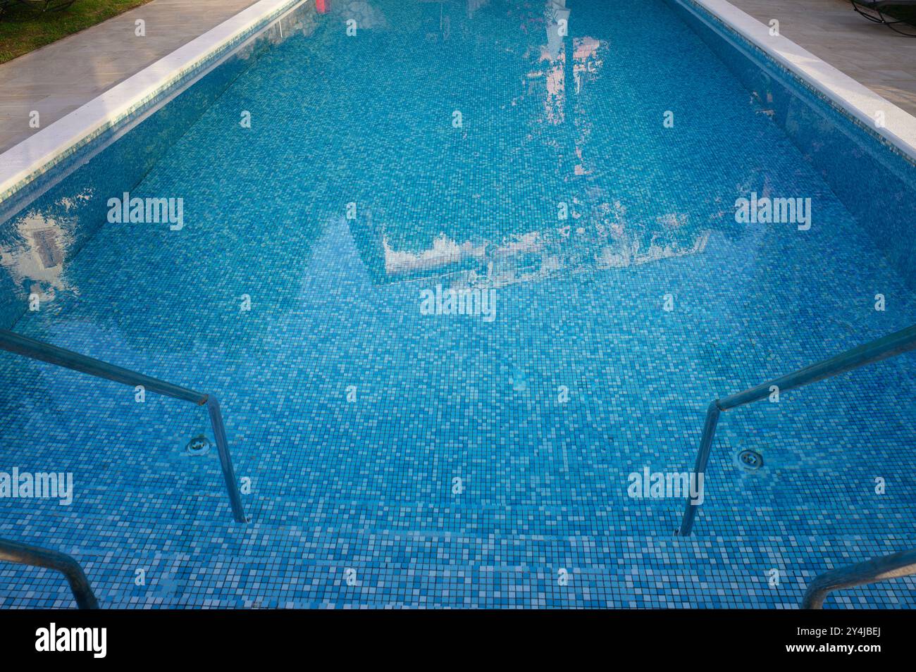 Swimming pool with stair and blue water. Grab bars ladder in the blue ...