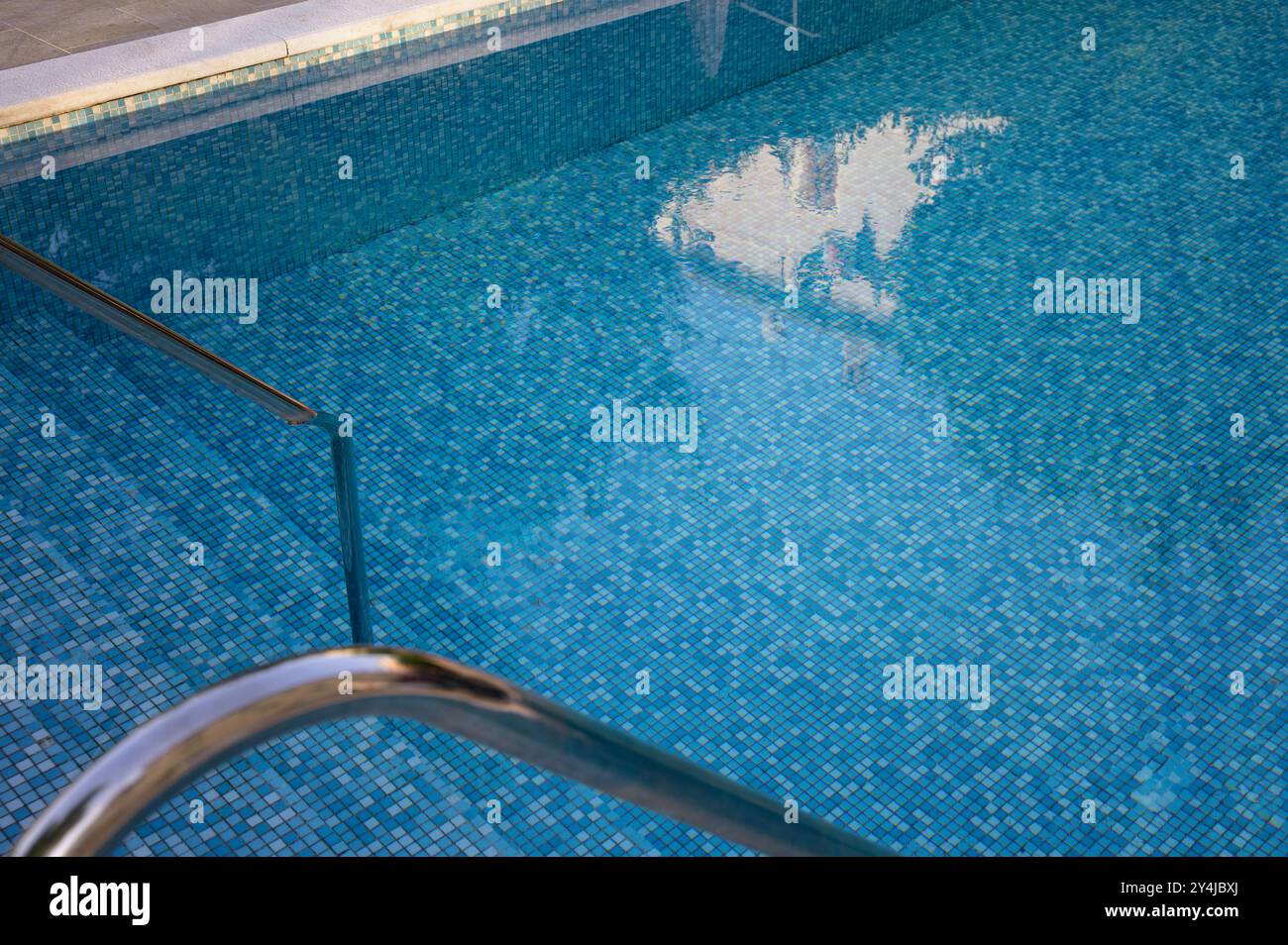 Swimming pool with stair and blue water. Grab bars ladder in the blue ...