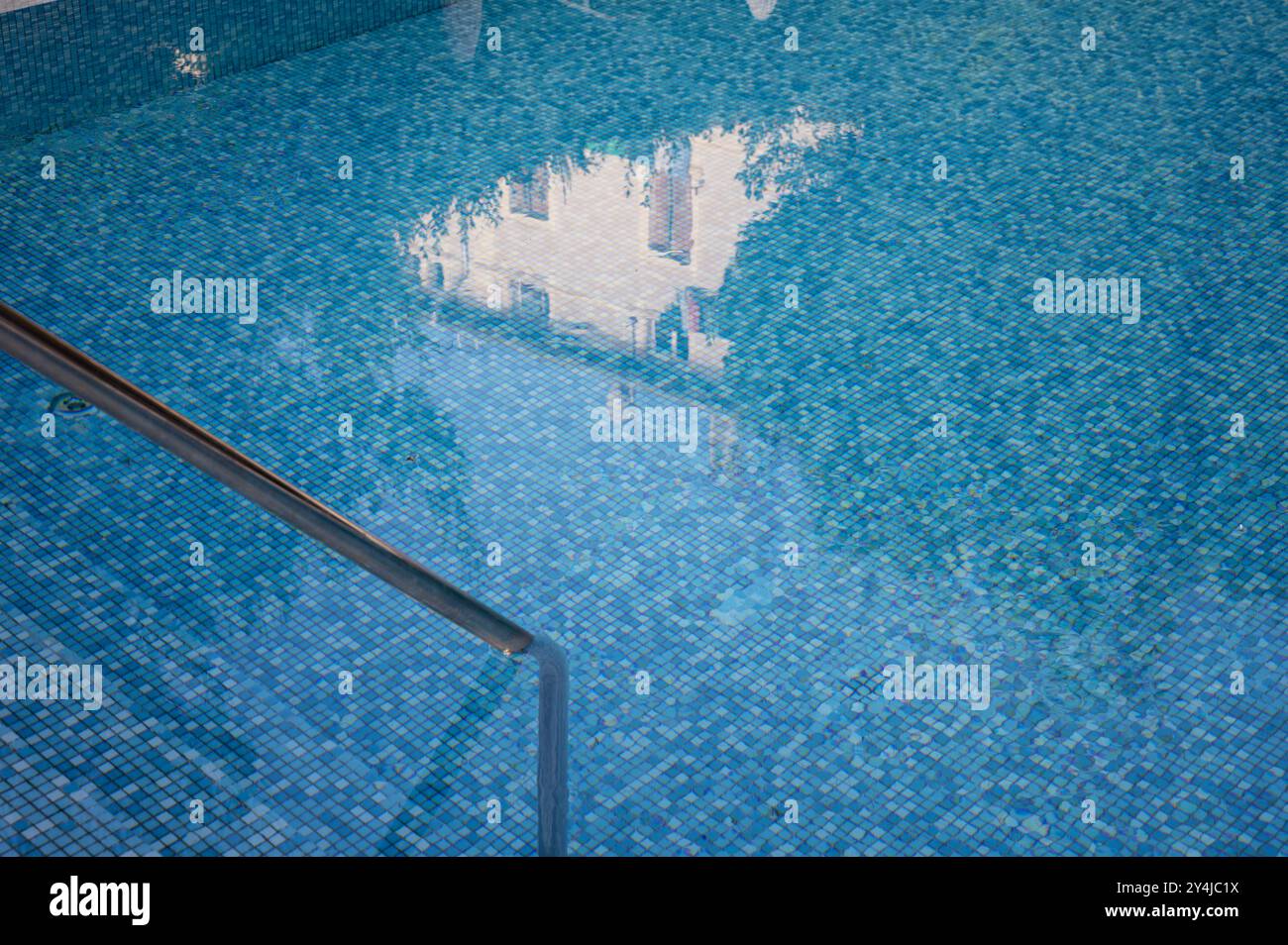 Swimming pool with stair and blue water. Grab bars ladder in the blue ...