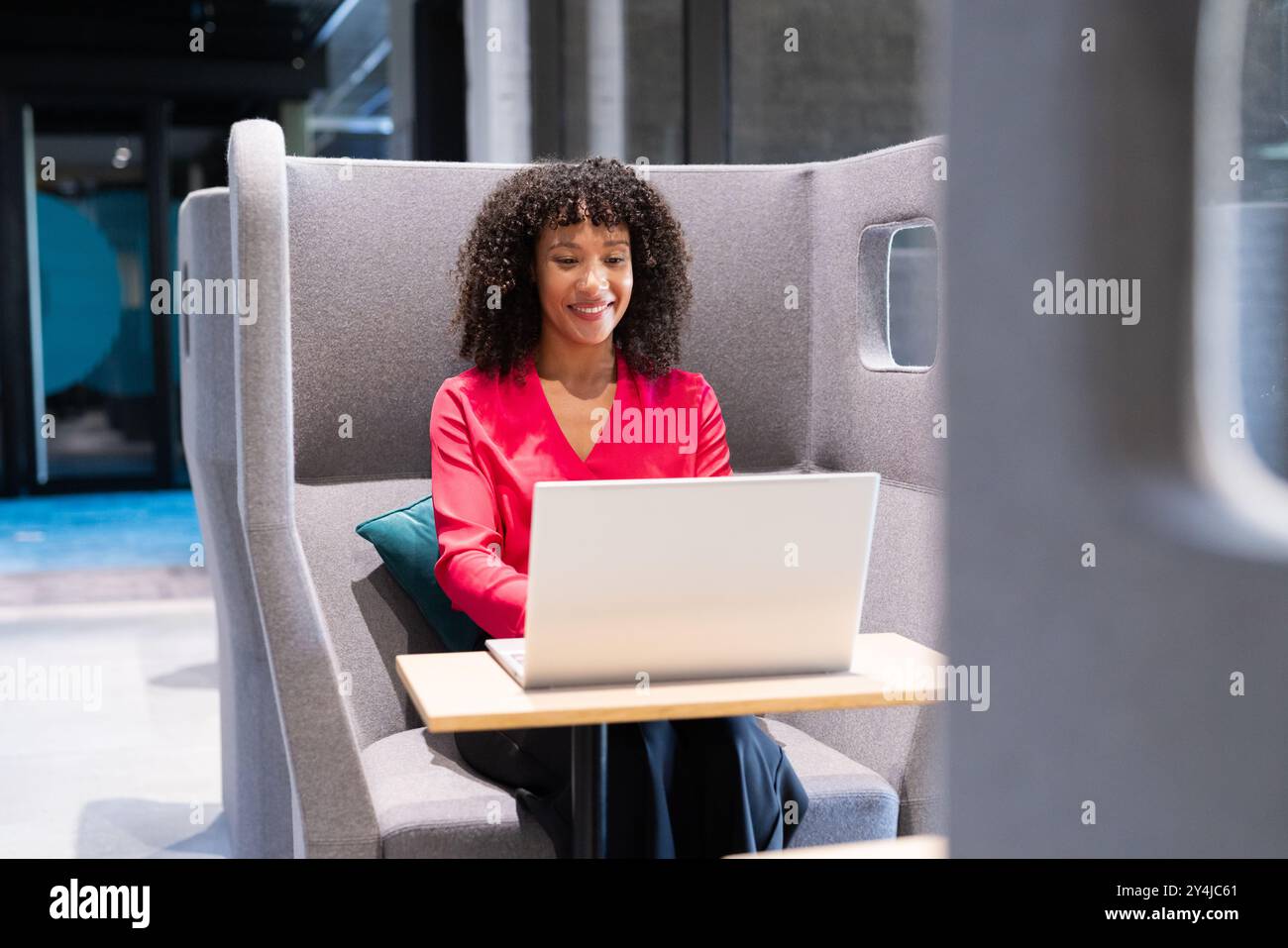 Working on laptop, woman sitting in modern office booth, smiling and ...