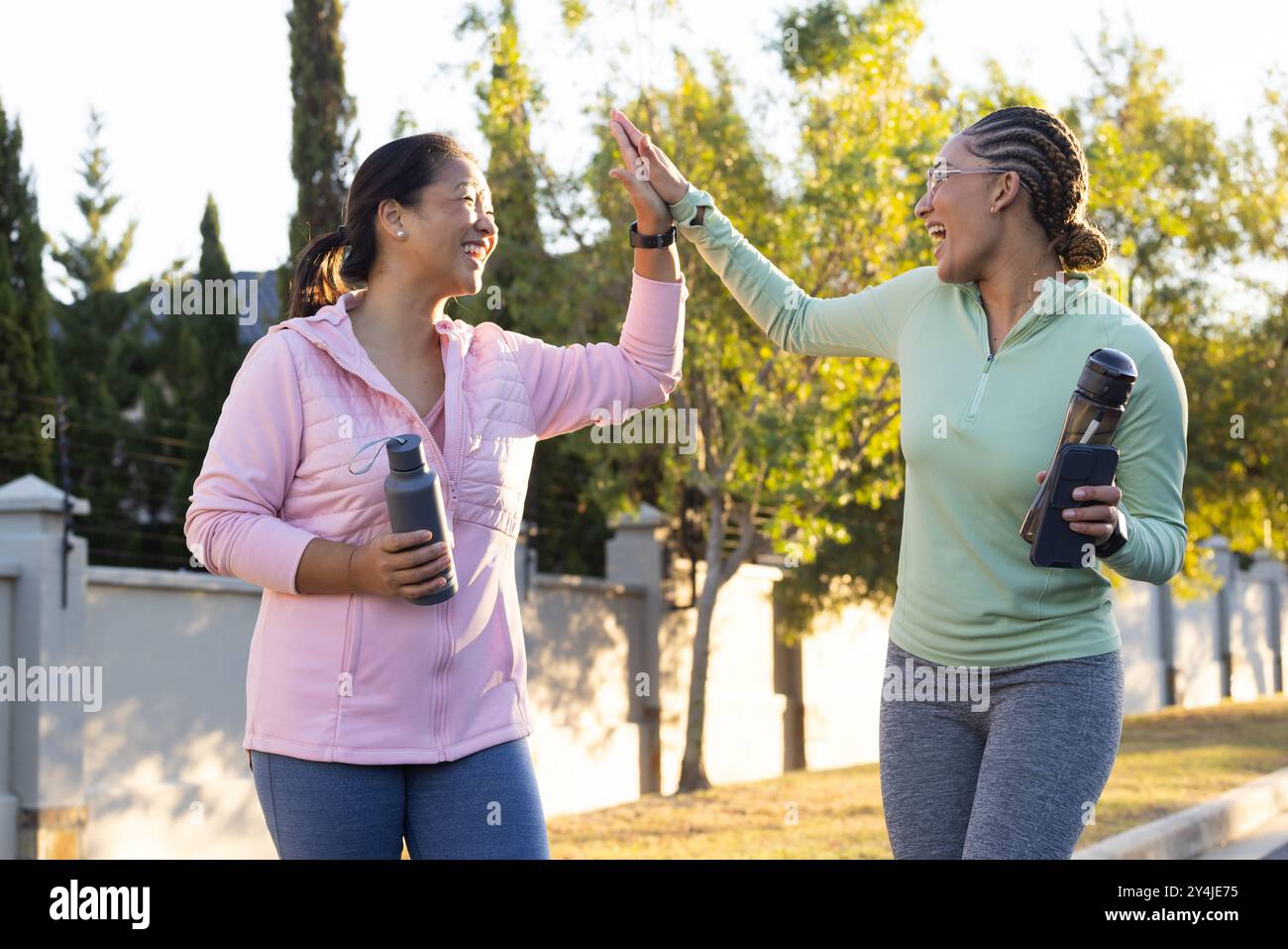 High-fiving, two women friends holding water bottles after outdoor ...