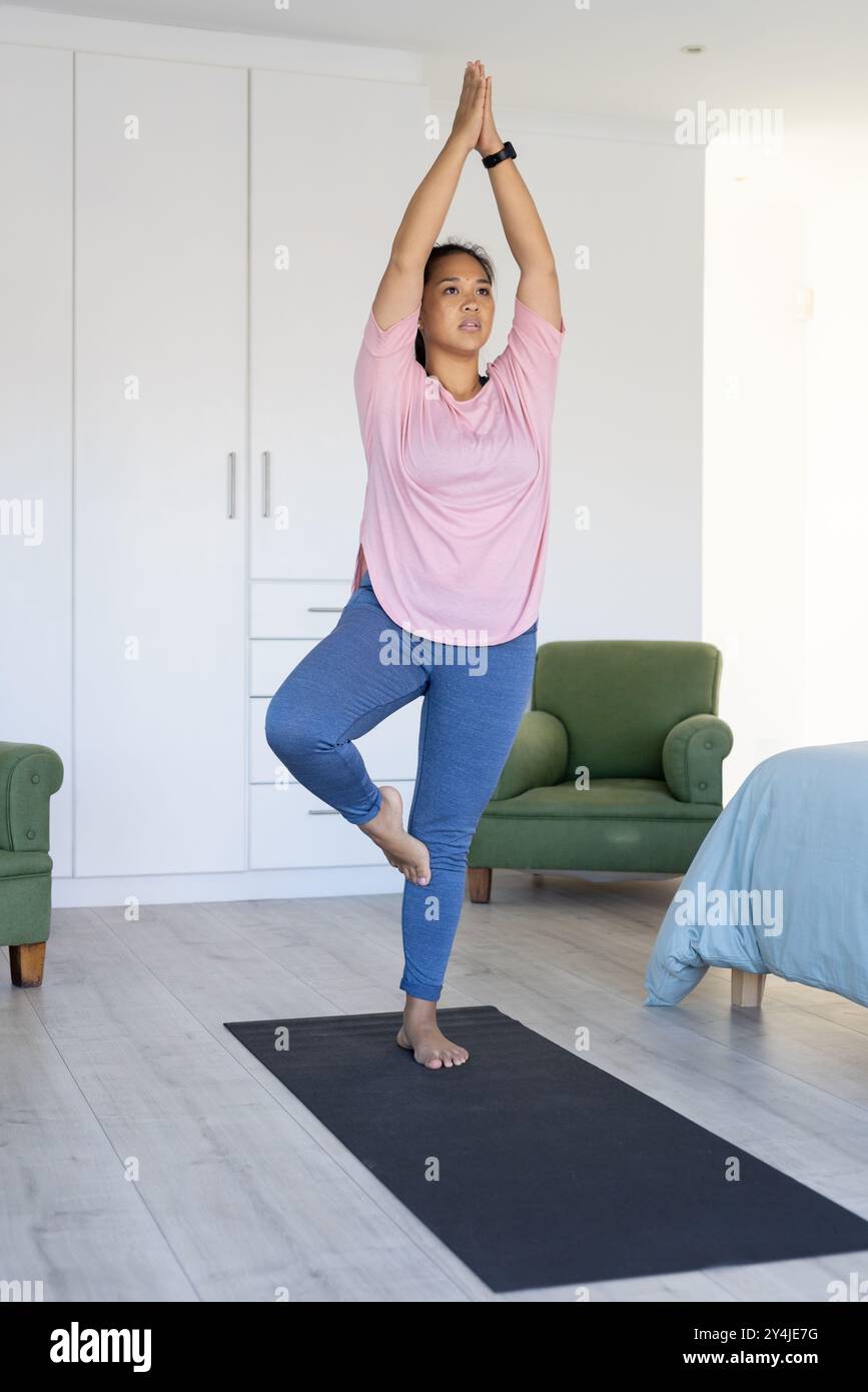 Practicing yoga, woman balancing on one leg on yoga mat in bedroom ...