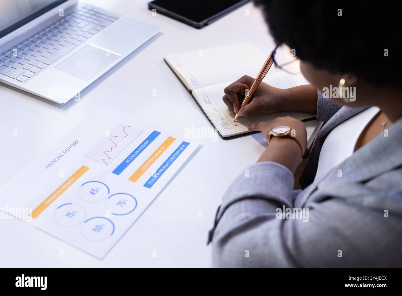 Writing in notepad, businesswoman analyzing annual report at office ...