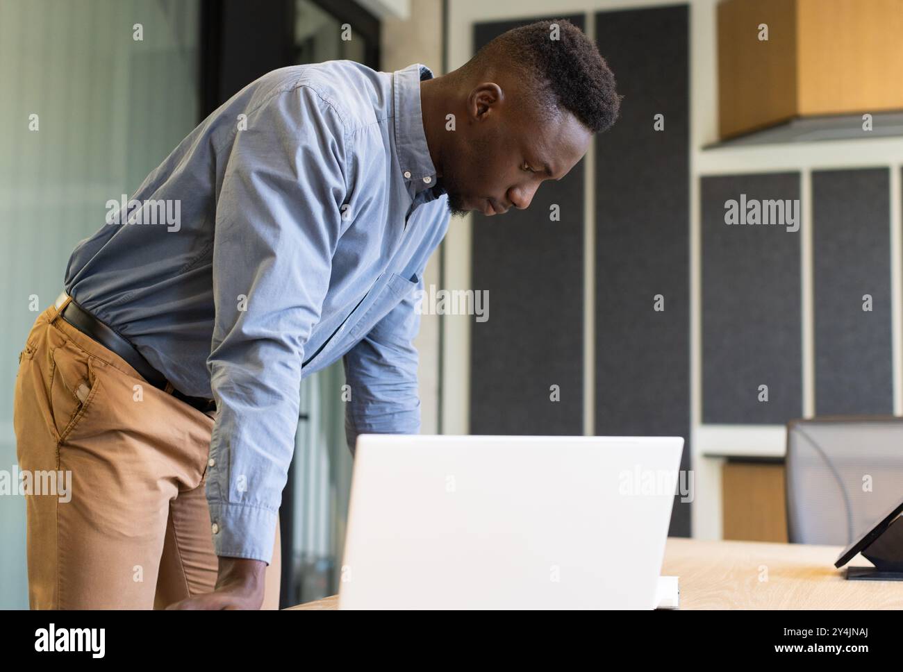 Working in office, man leaning over desk and focusing on laptop screen ...