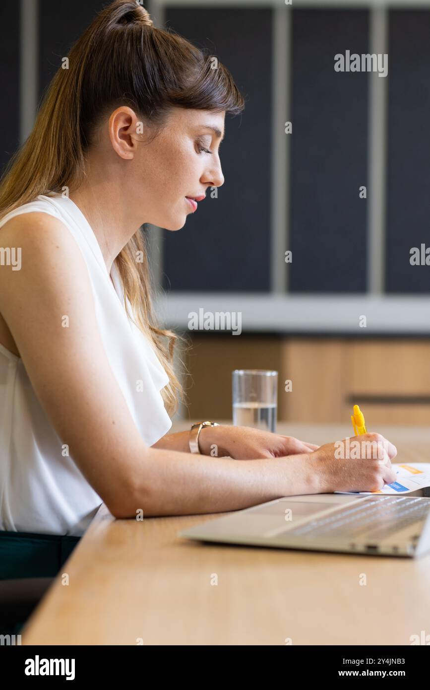 Writing notes, woman working at desk with laptop and glass of water ...