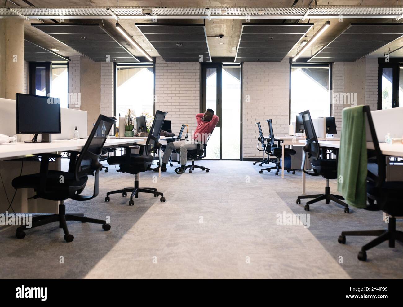 Working in modern office, man stretching at desk with computer monitors ...