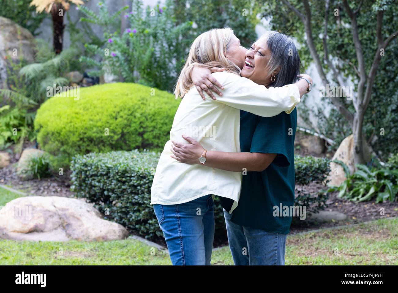 In garden, hugging and laughing, two senior multiracial female friends ...