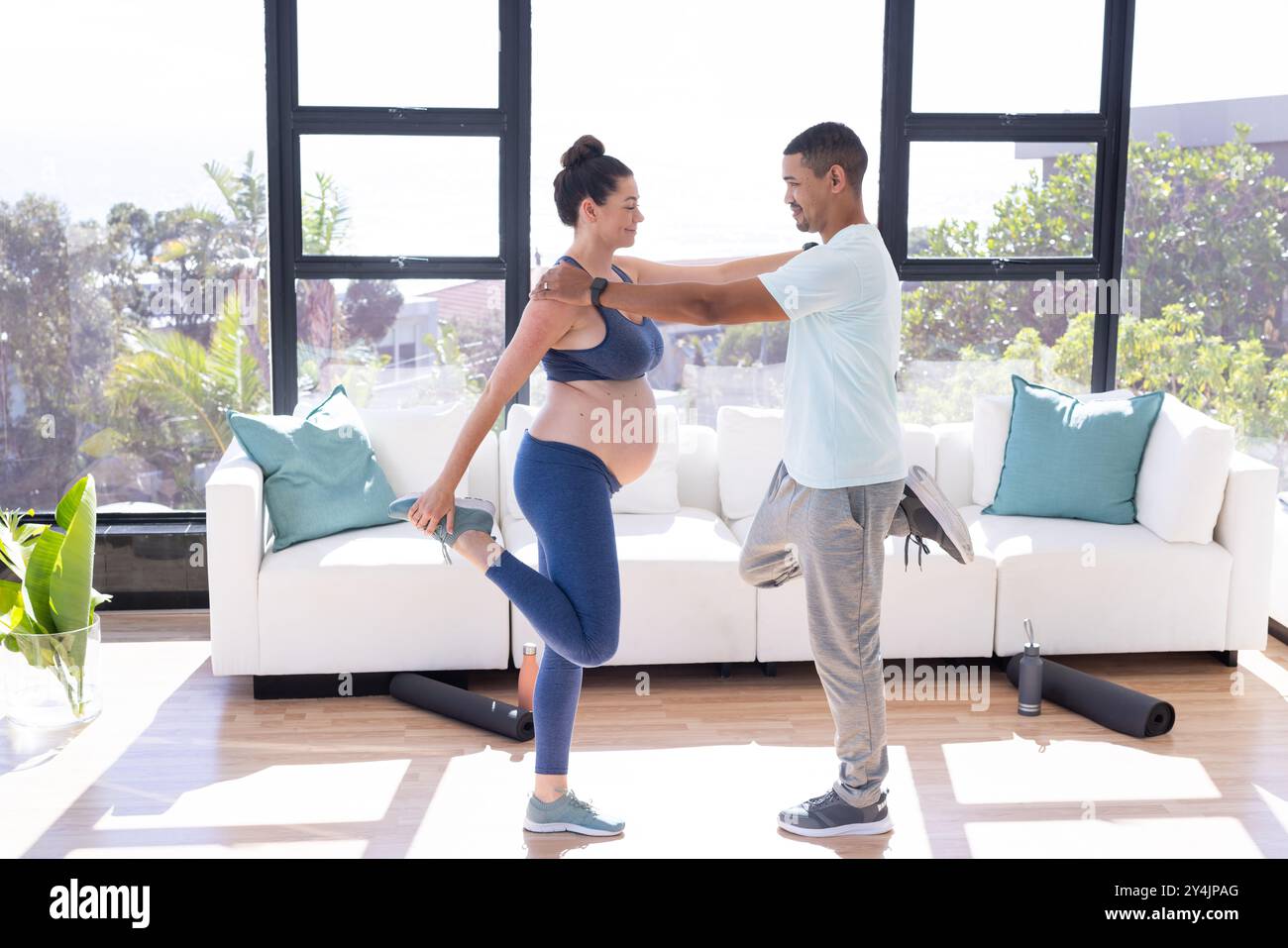 At home, Pregnant multiracial couple doing yoga together in living room ...