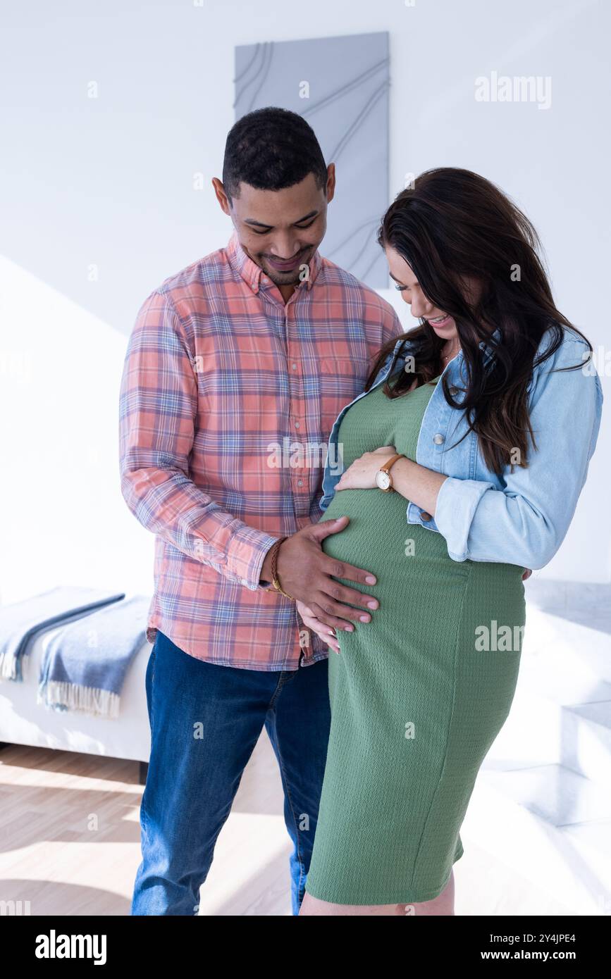 At home, Expecting multiracial couple smiling, man touching woman's ...