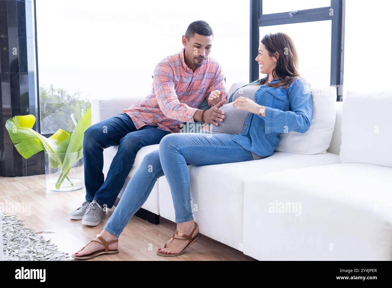 At home, Expecting multiracial couple sitting on couch, man touching ...