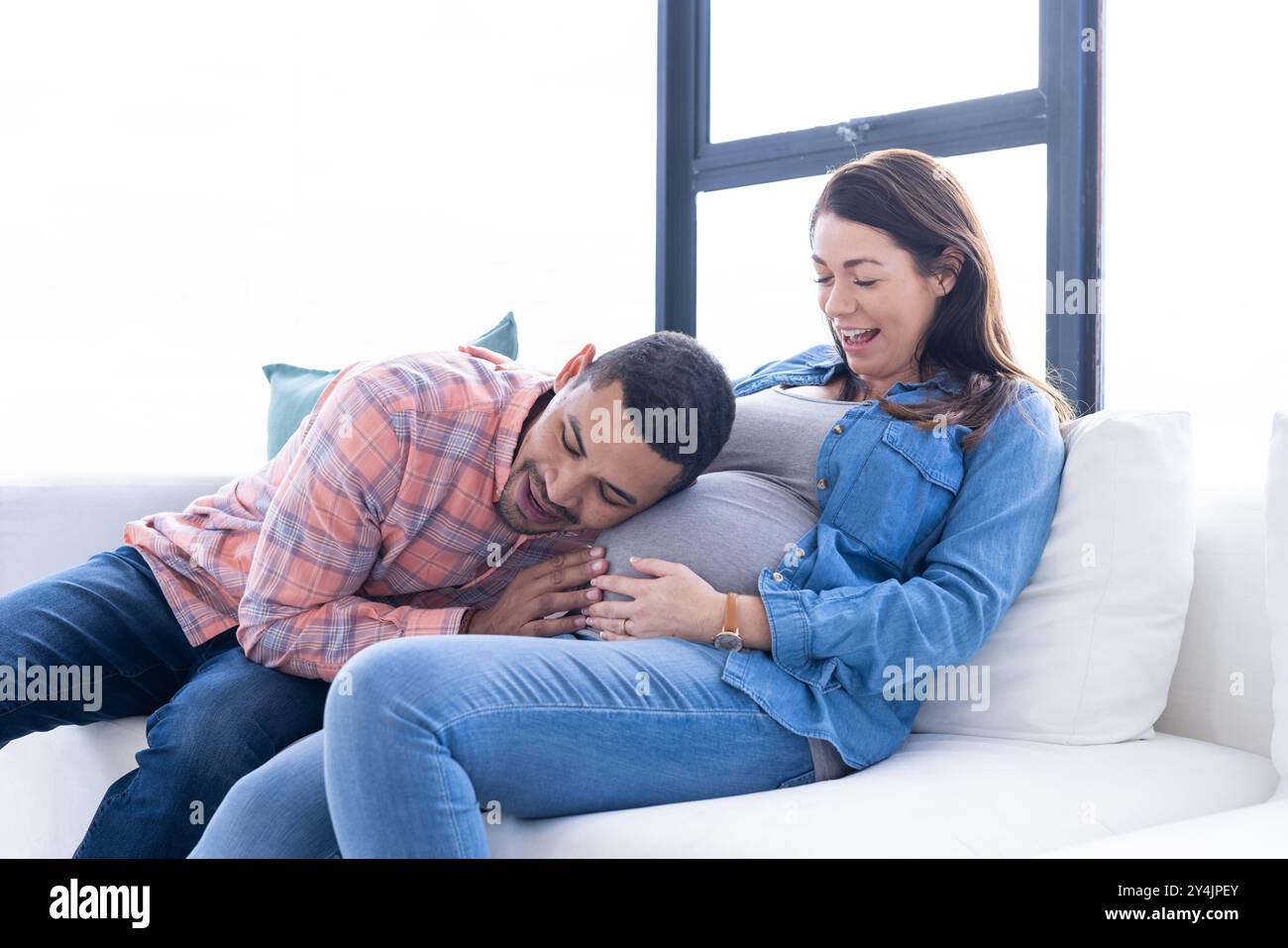 At home, multiracial couple, expectant father listening to pregnant ...
