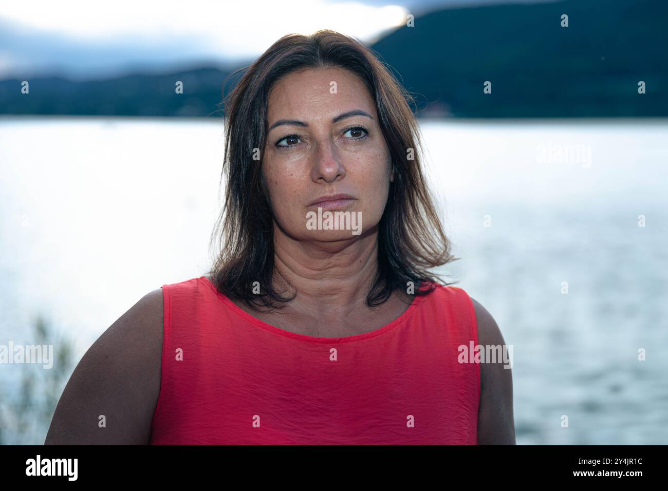 Thoughtful woman by calm lake, serene expression, nature background, outdoor portrait, sunset ...