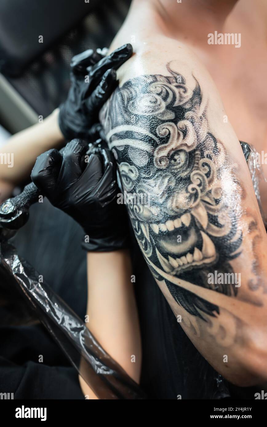 professional woman artist making stylish black tattoo of Japanese demon ...
