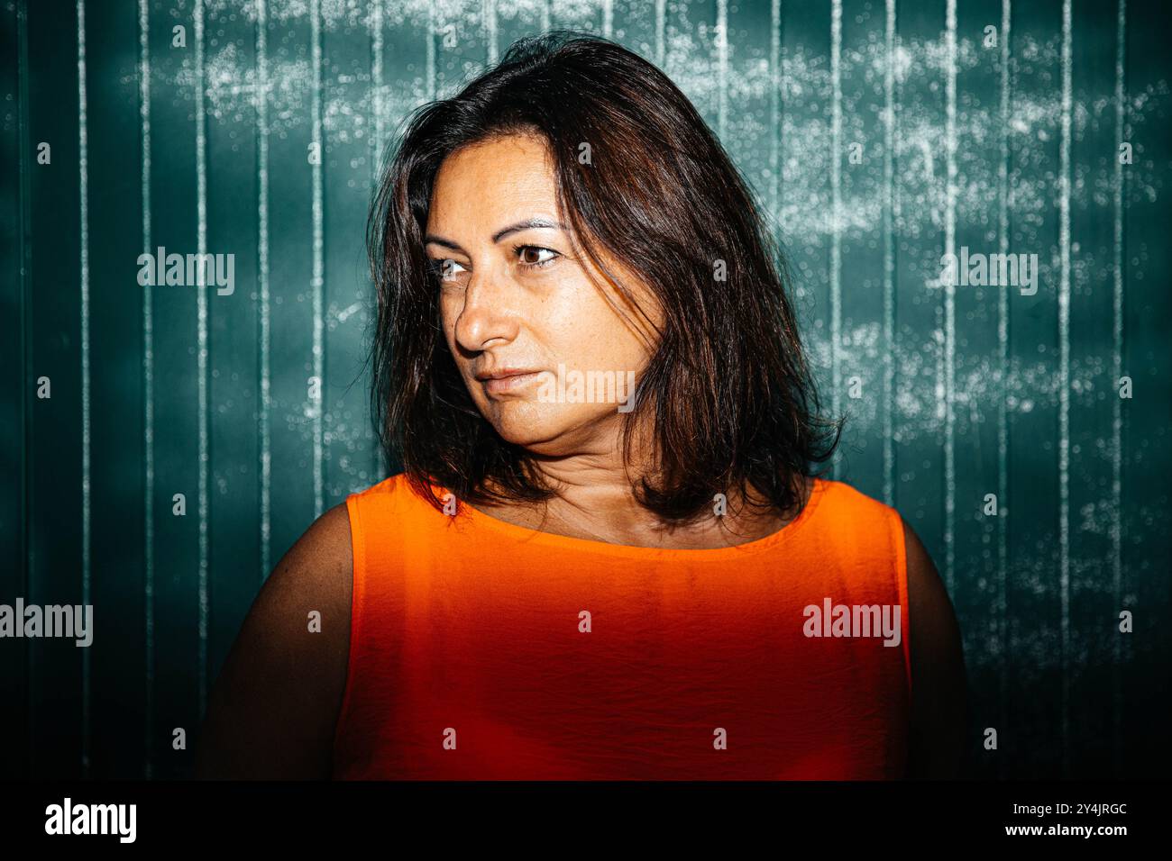 Woman's portrait wearing orange top, shadows on green background ...