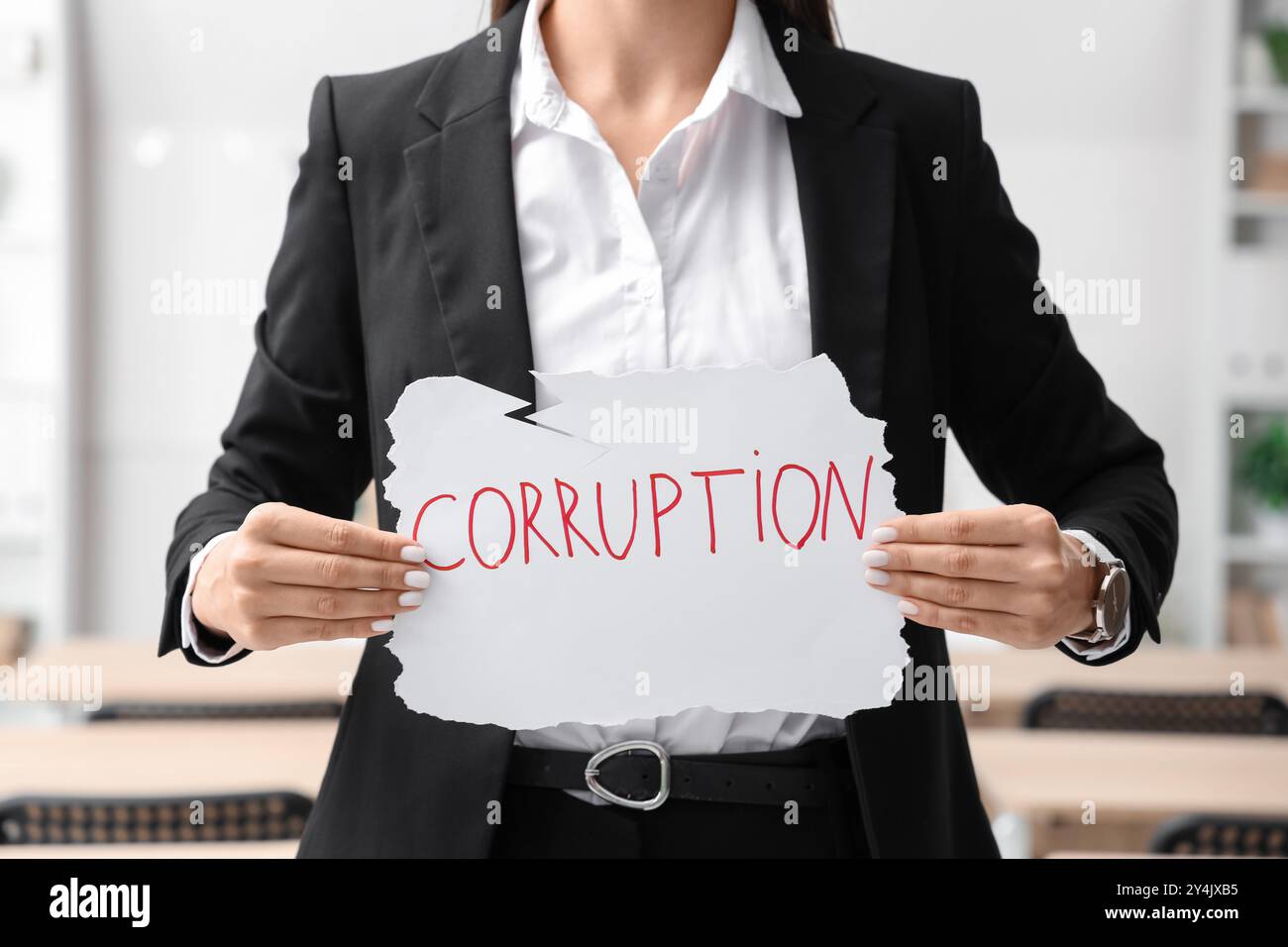 Female teacher holding paper with word CORRUPTION in classroom, closeup ...