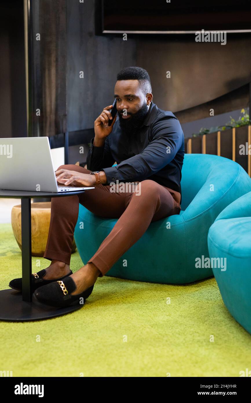 Using laptop and making phone call, African american African american man working from office on ...