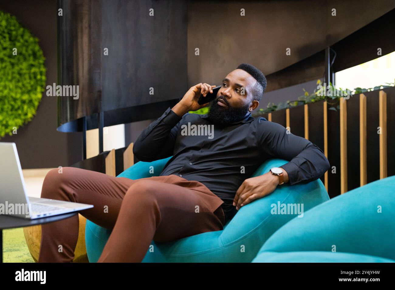Talking on smartphone, African american man sitting on bean bag with ...