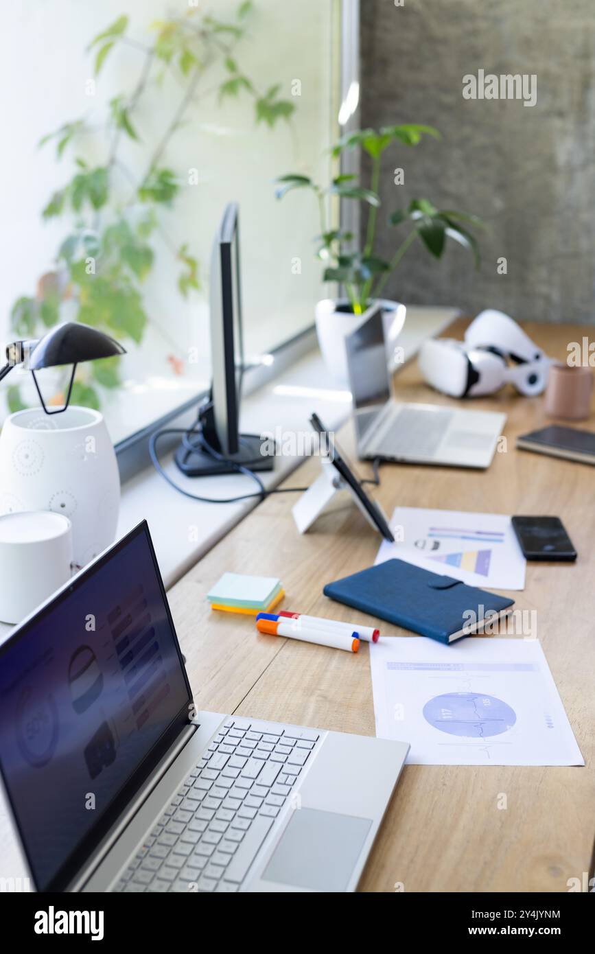 Office workspace with laptops, documents, and VR headset on wooden desk ...