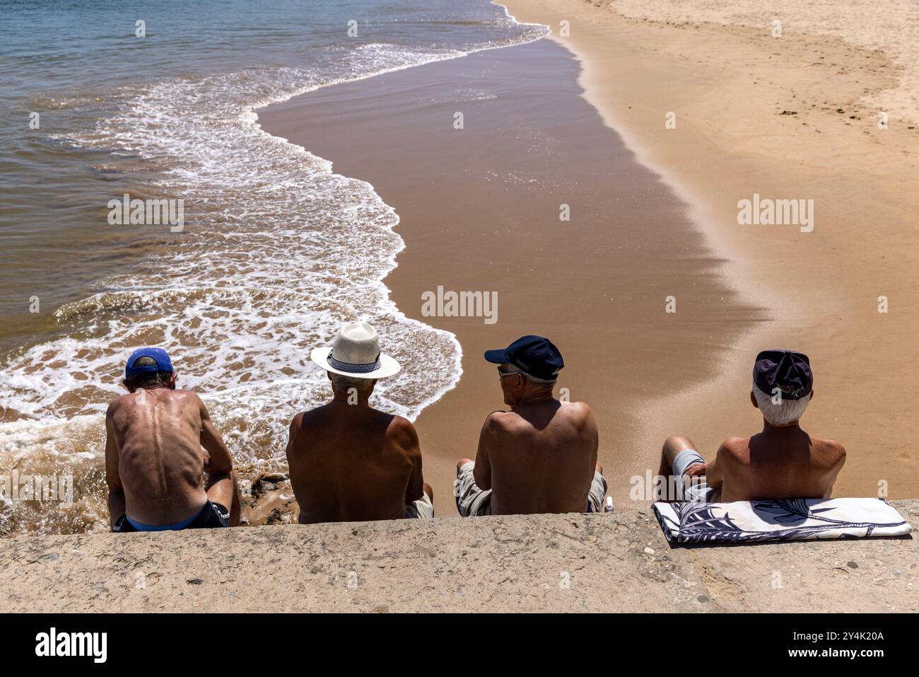 Four elderly men sit on a ledge overlooking the beach in Cascais ...