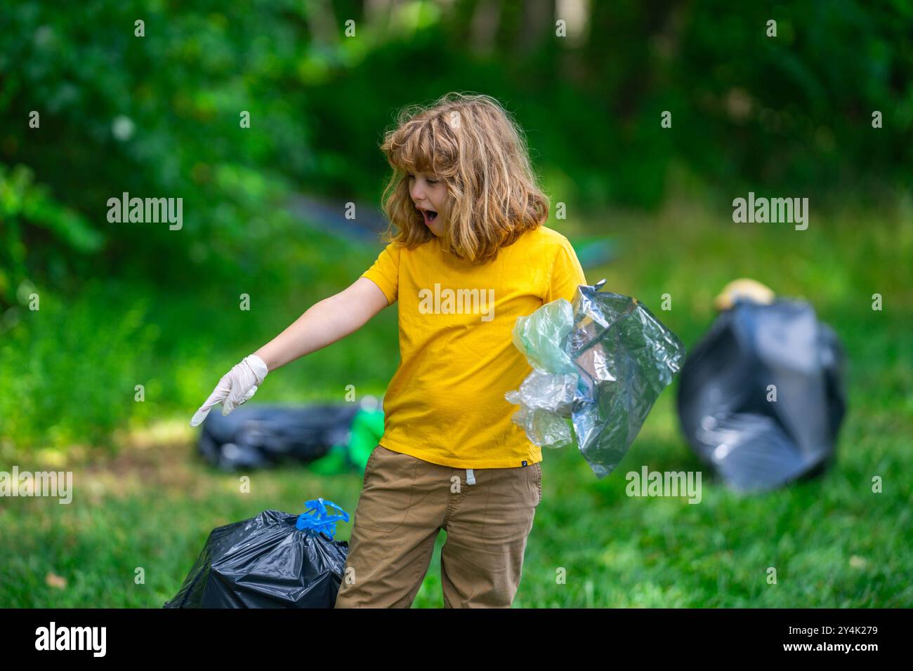 Kid in rubber gloves with trash bag clean up garbage on forest outdoor ...