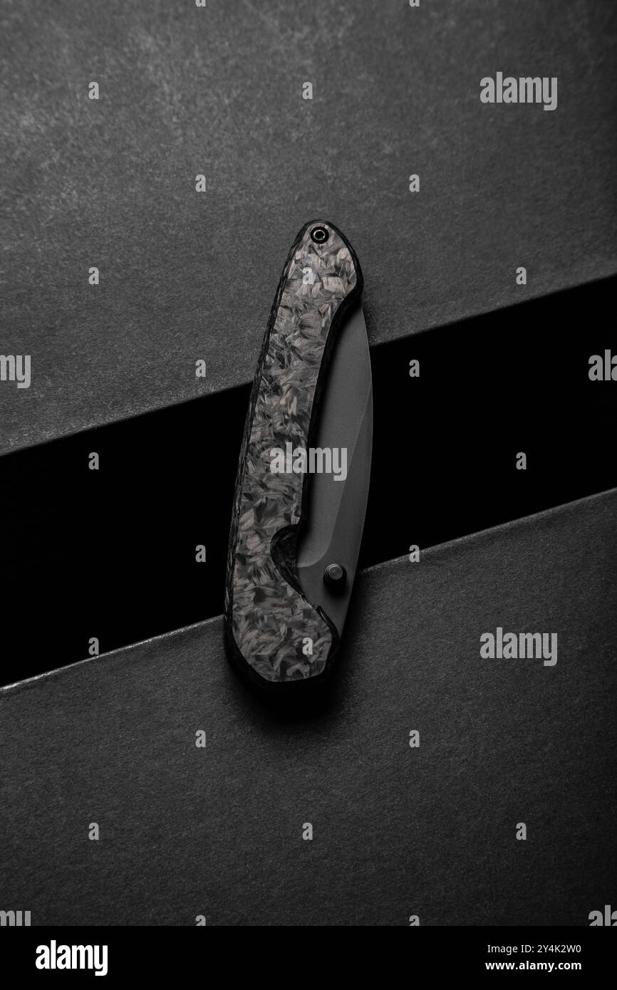 Minimalistic photo of a folding knife on a dark, textured surface. The ...