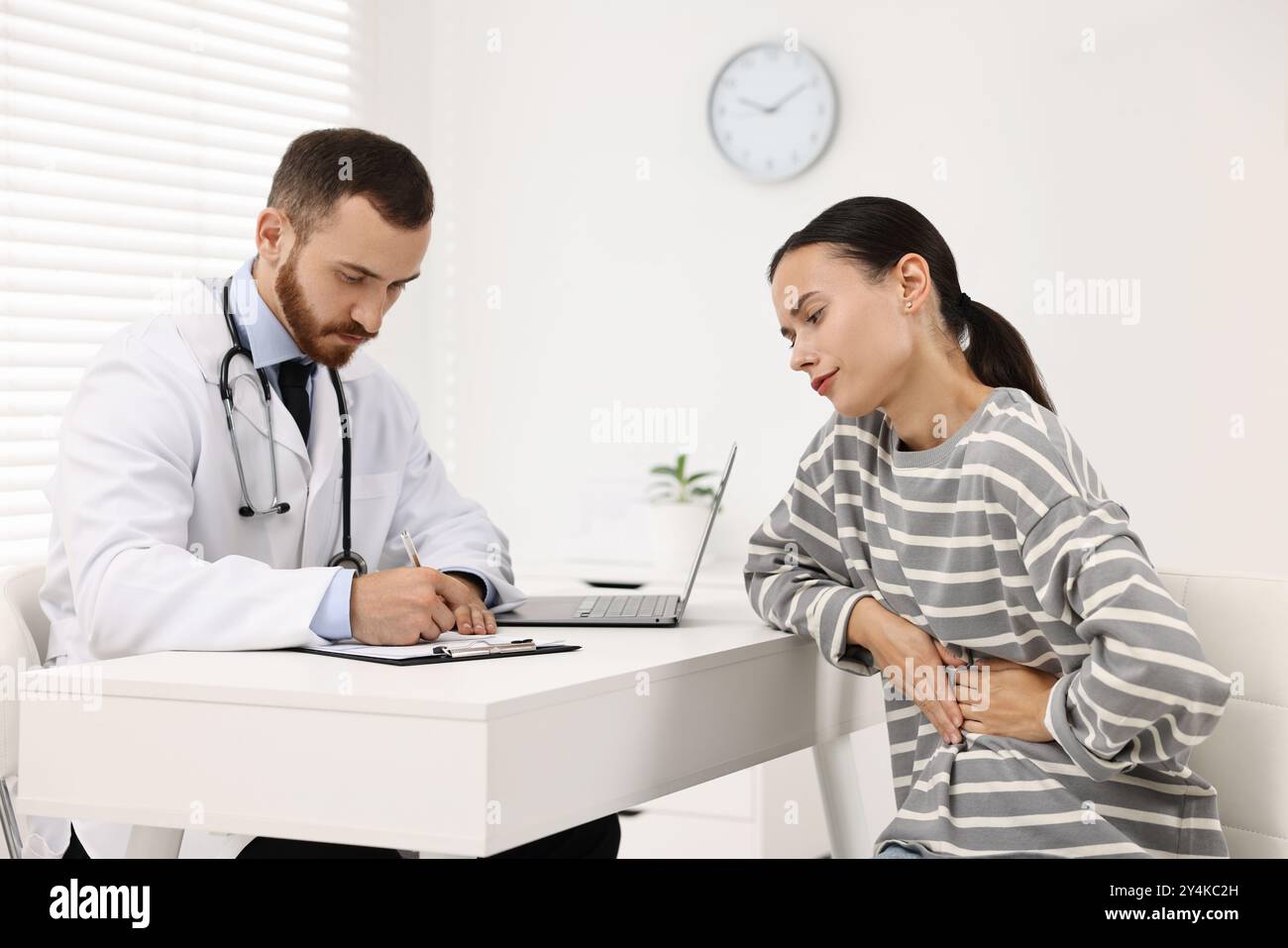 Doctor consulting patient with stomach pain at table in hospital Stock ...