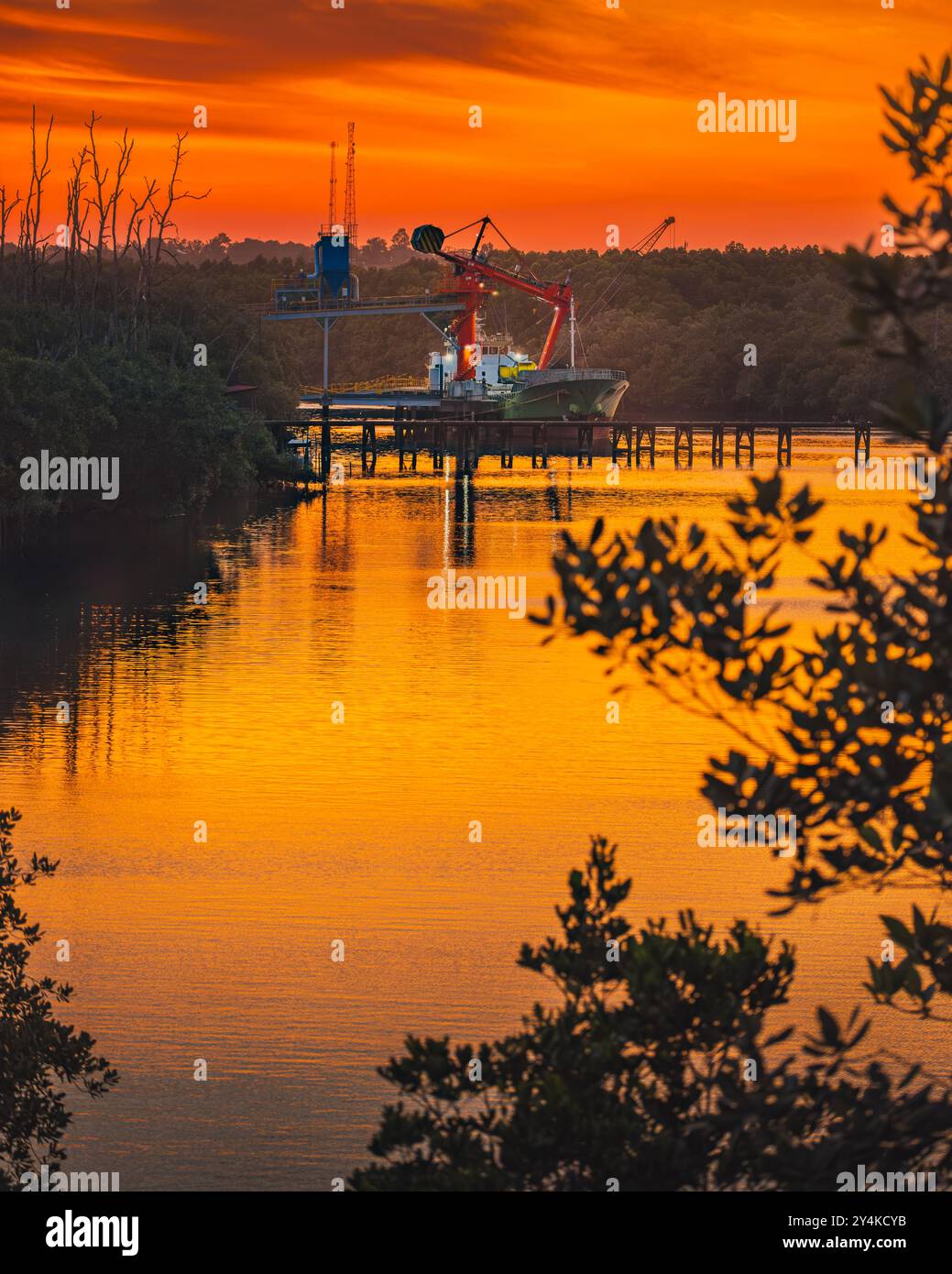 A peaceful river reflects the fiery sunset, illuminating the cargo ship ...