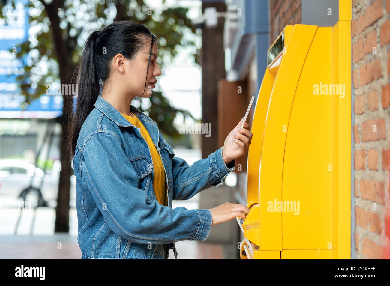 A side view of a beautiful Asian woman in a denim jacket inserting her ...