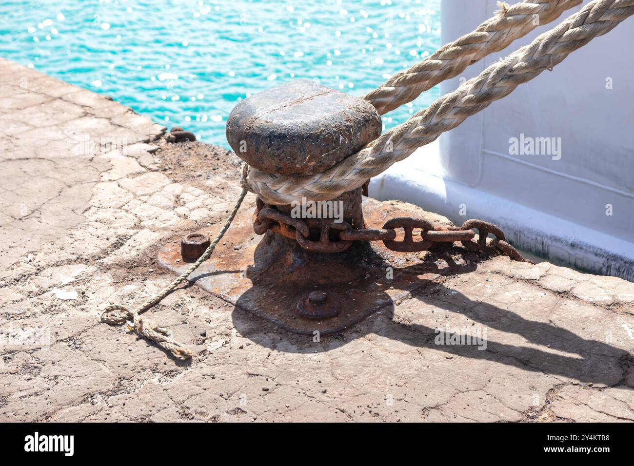 Rusty anchor is tied to a chain. The chain is tied to a metal post. The ...