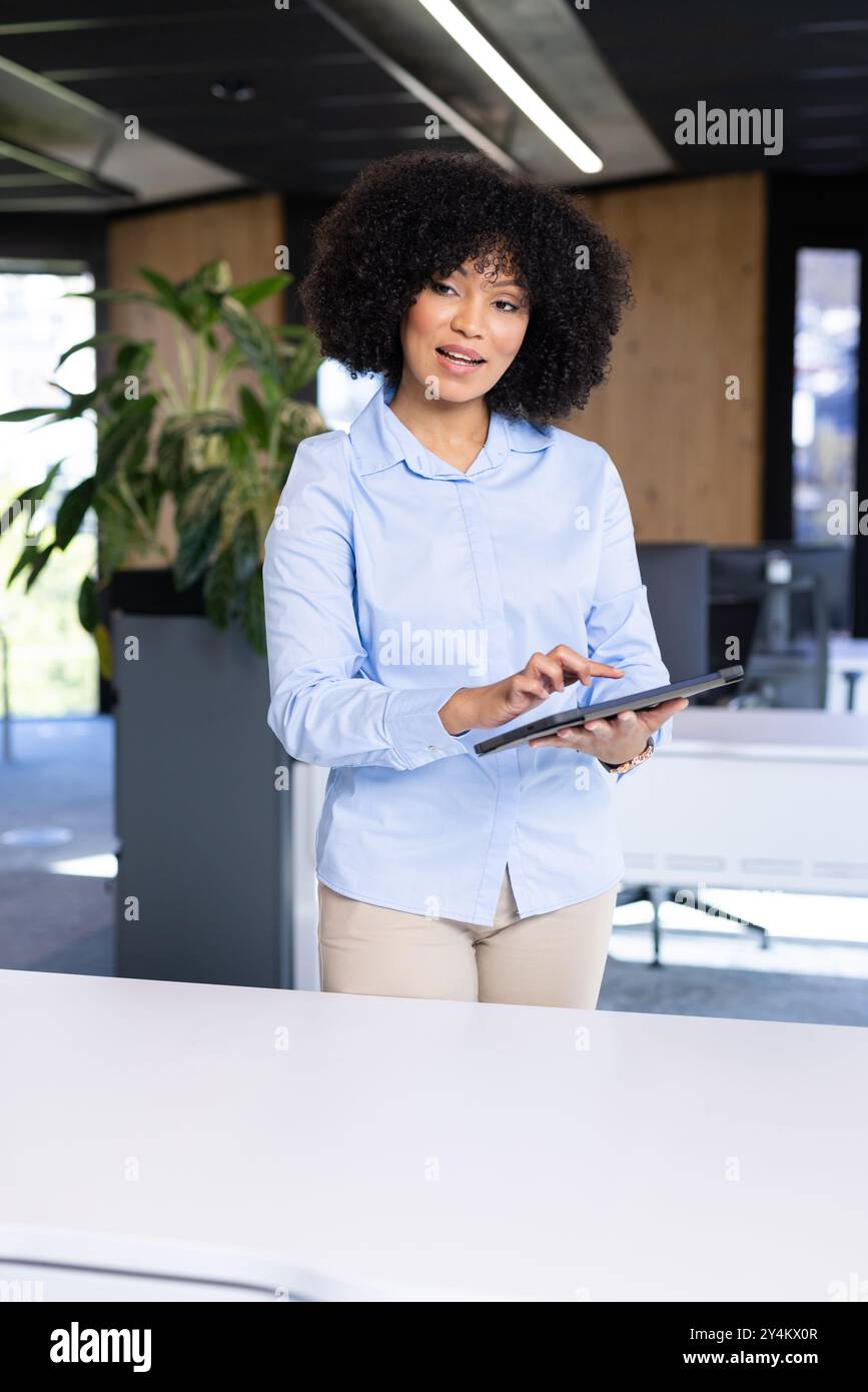 Using tablet, businesswoman standing in modern office, focusing on work ...