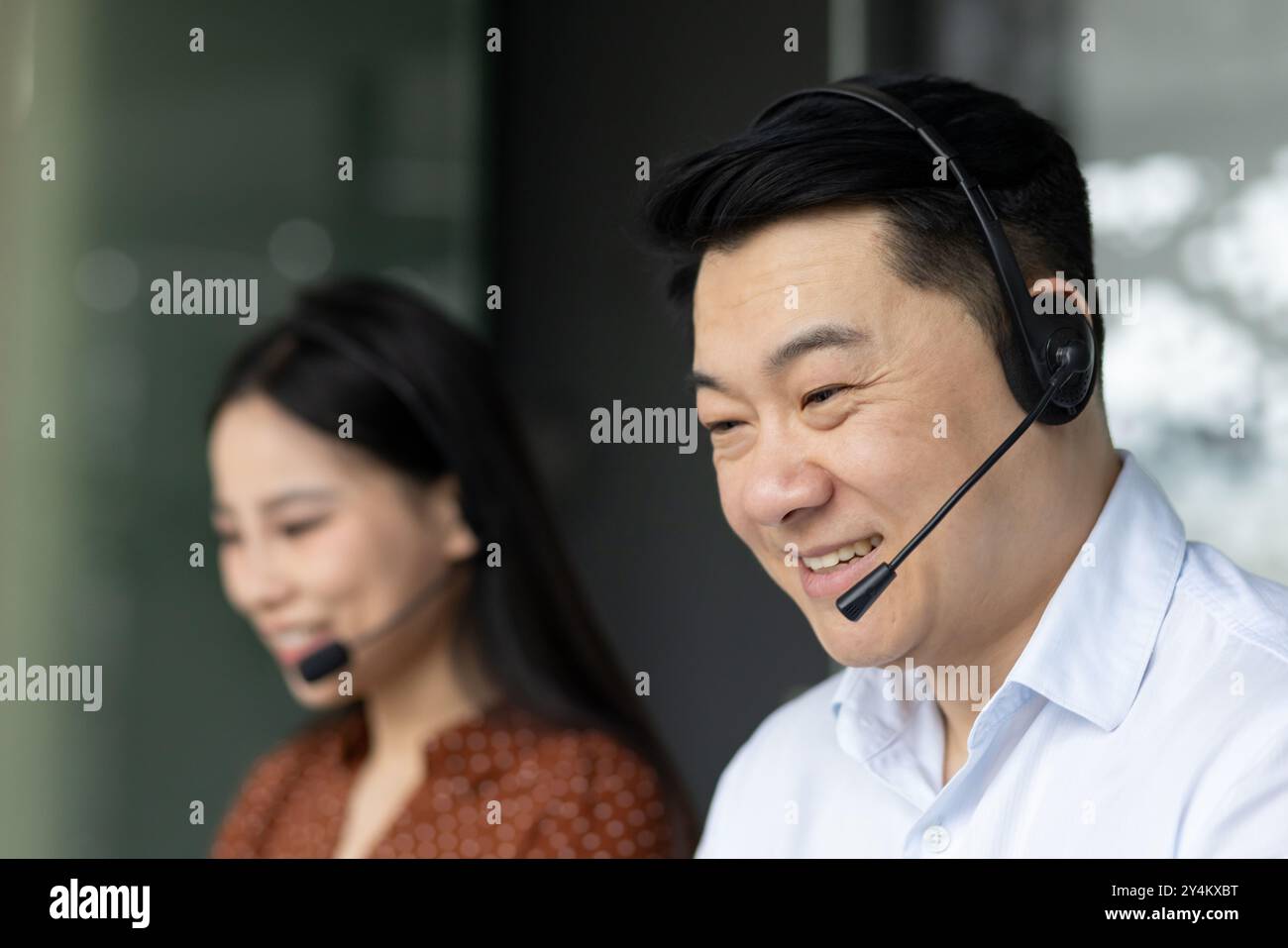 Smiling Asian customer service professionals wearing headsets engaging ...