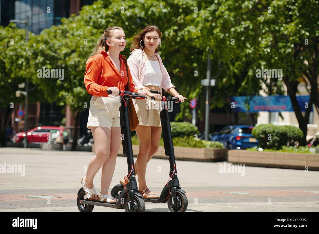 Two Young Women Riding Electric Scooters in Urban Area Stock Photo - Alamy
